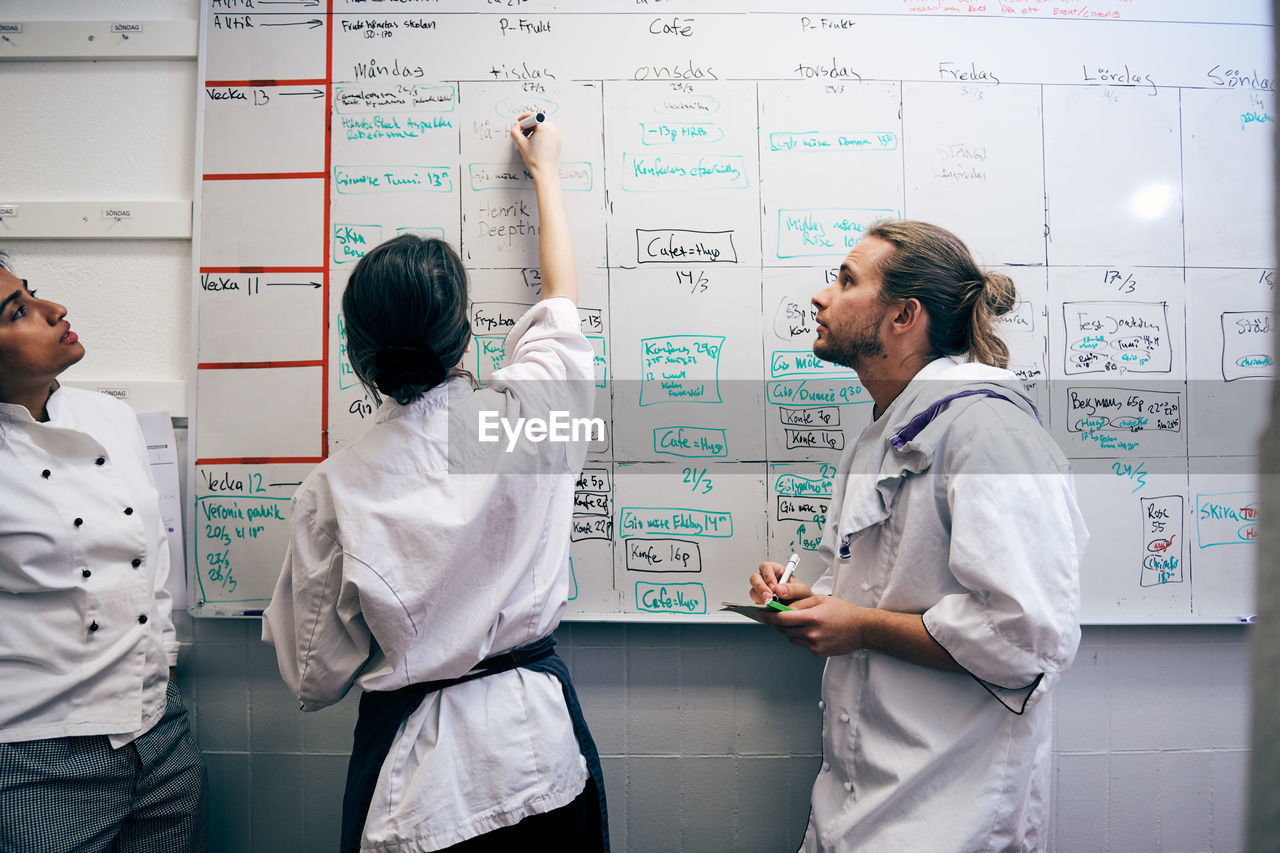 Female chef writing menu on whiteboard by | ID: 132811882