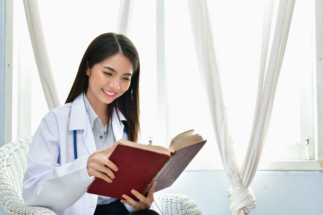 Smiling female doctor reading book at office | ID: 143477582