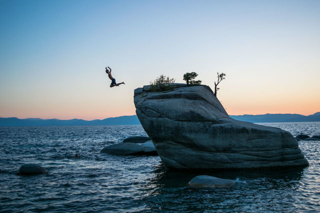 Man jumping off of rock by sea against | ID: 106274346